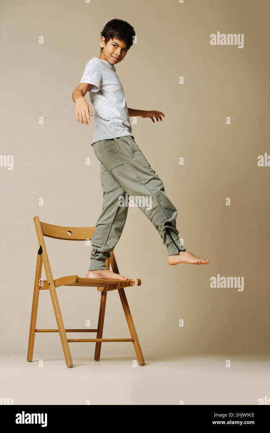 Cool indian boy balancing on one leg on a wooden folding chair in a ...