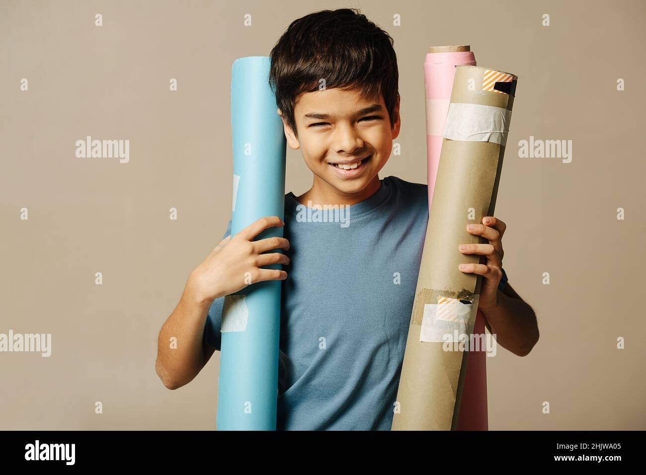 Cheeky indian boy holding colored rolls of backdrops fixed with a tape ...
