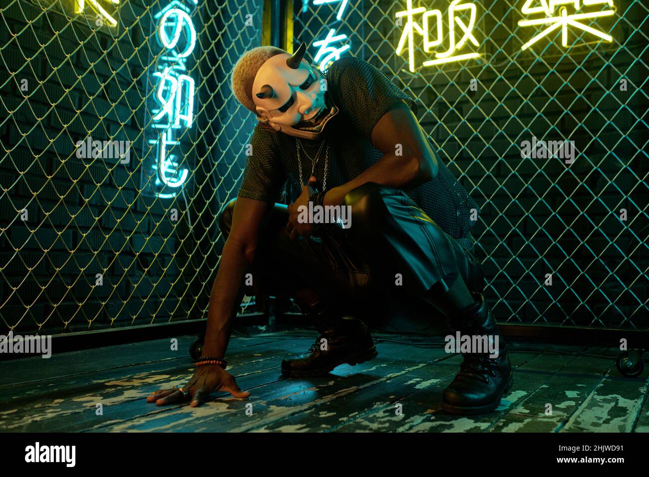 Young African man in mask of evil sitting on squats and touching floor ...