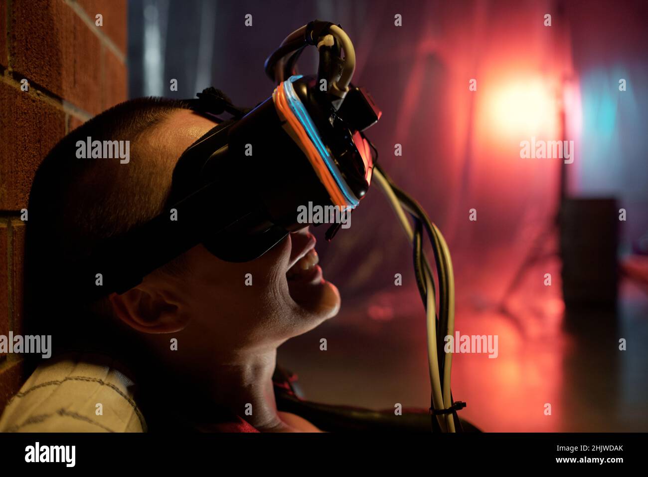 Happy cyberpunk girl with cyber reality headset sitting in dark hacker ...