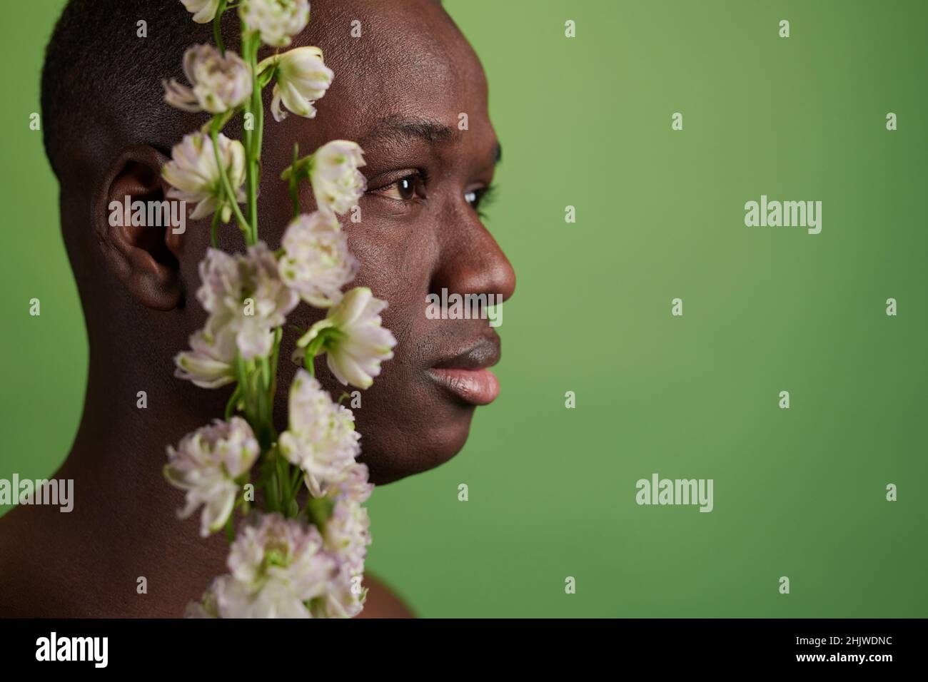Side view of head of black man with white flowers looking forwards ...