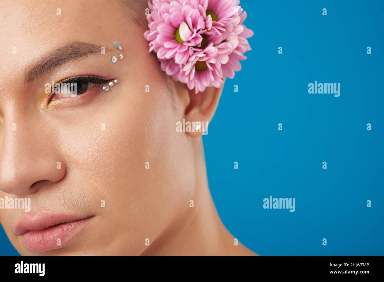 Face of serious young man with eye makeup, rhinestones on face and ...