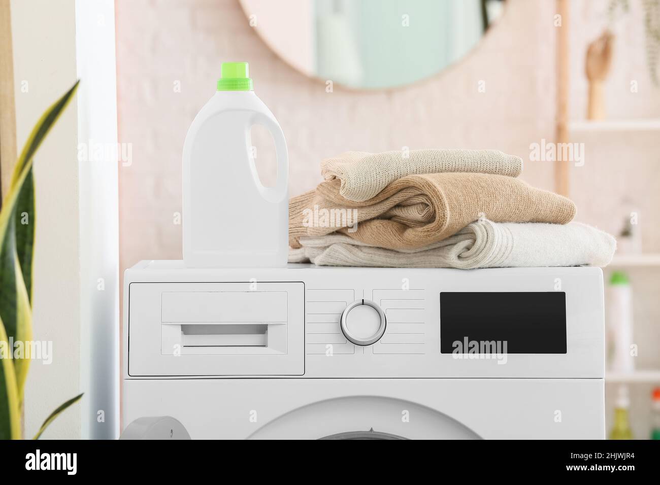 Stack of clean sweaters and detergent bottle on washing machine in ...