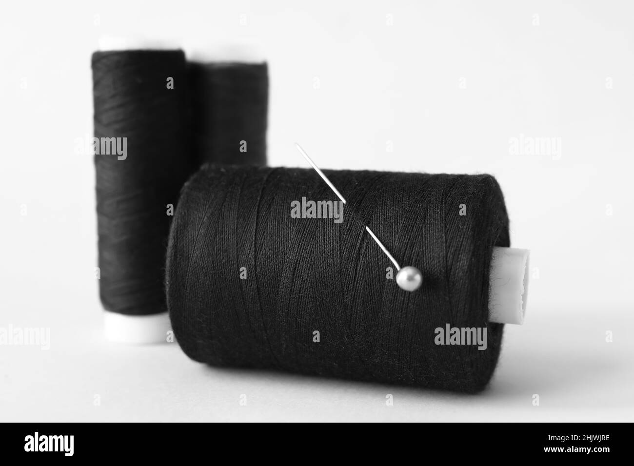 Black sewing thread spools with pin on white background Stock Photo - Alamy