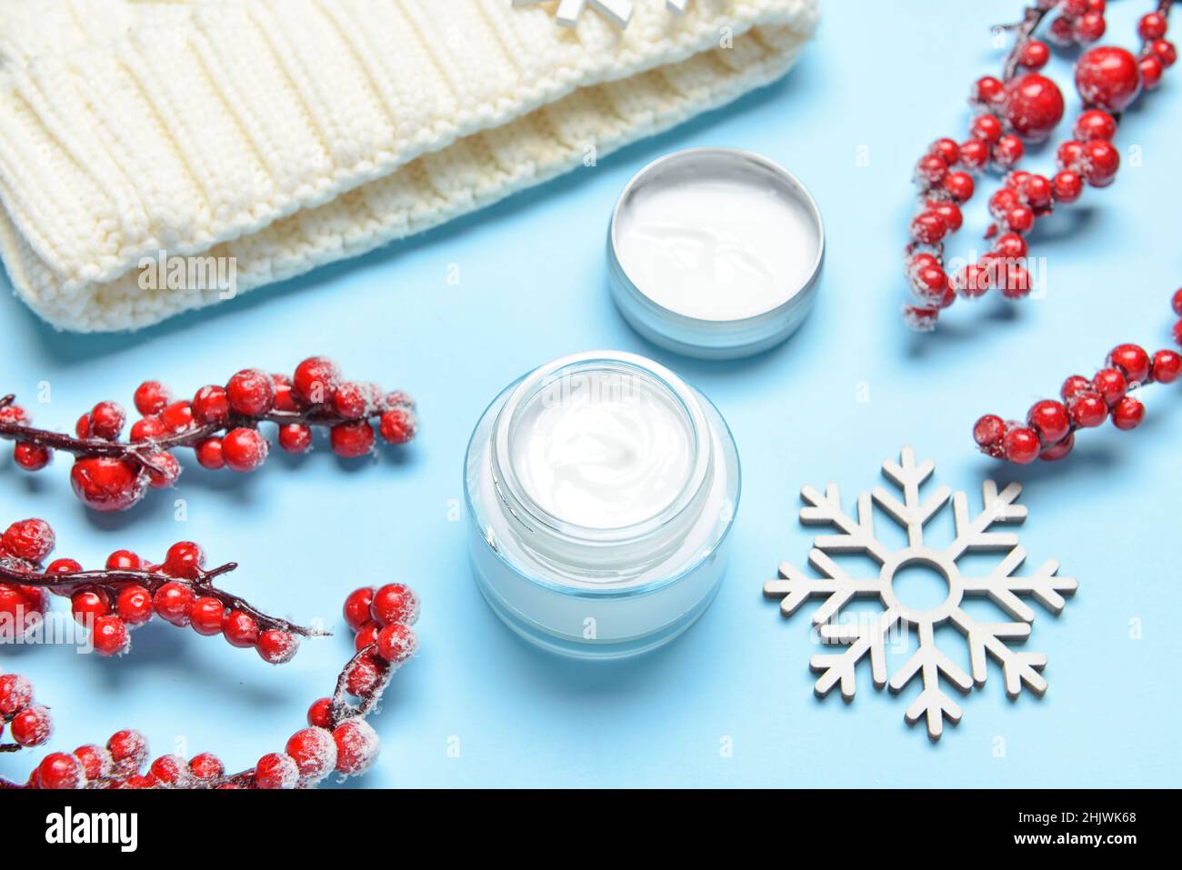 Jars with cream, winter decor and knitted hat on color background Stock ...