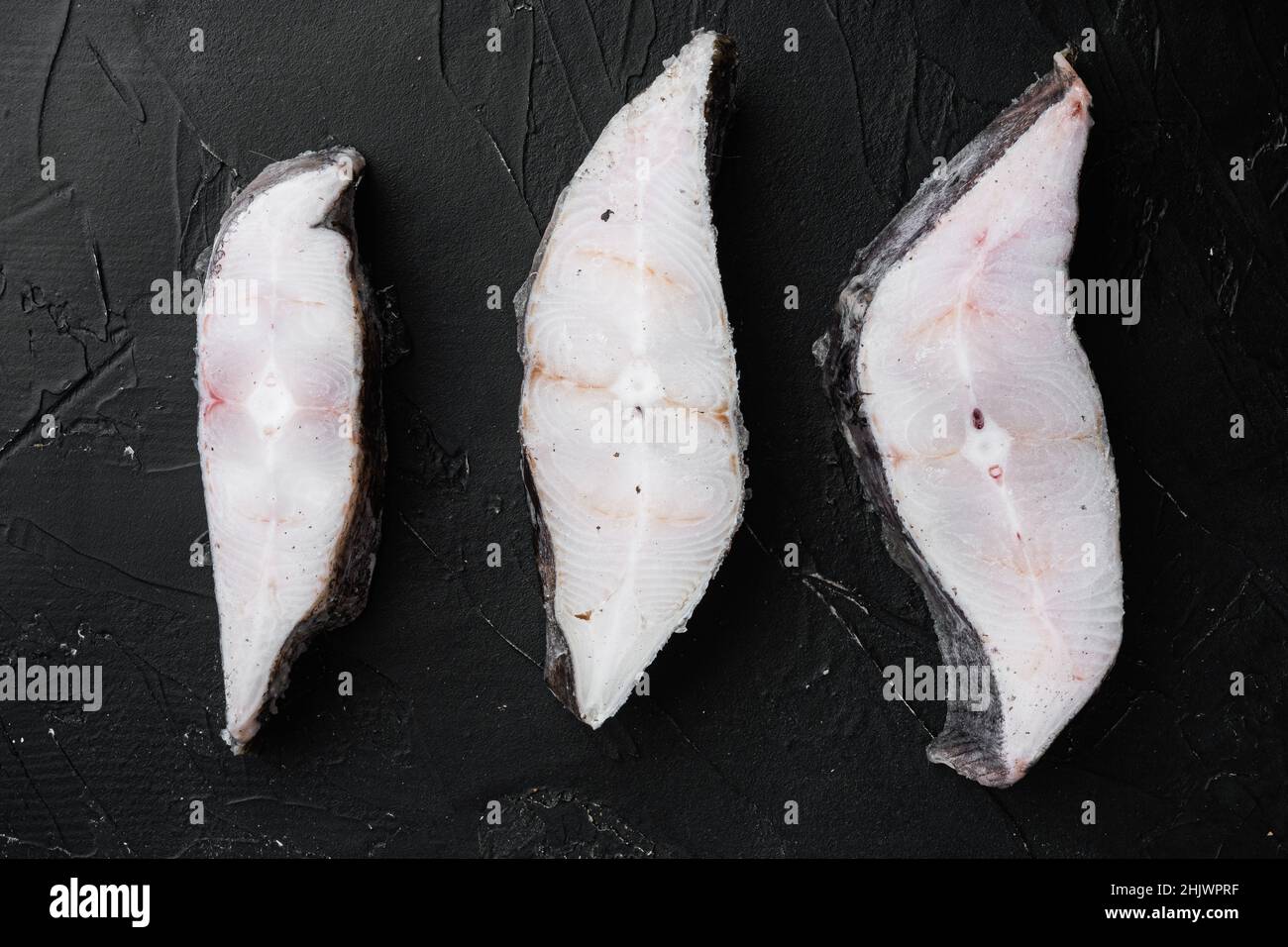 Frozen fillets of white fish, pollock set, on black dark stone table ...