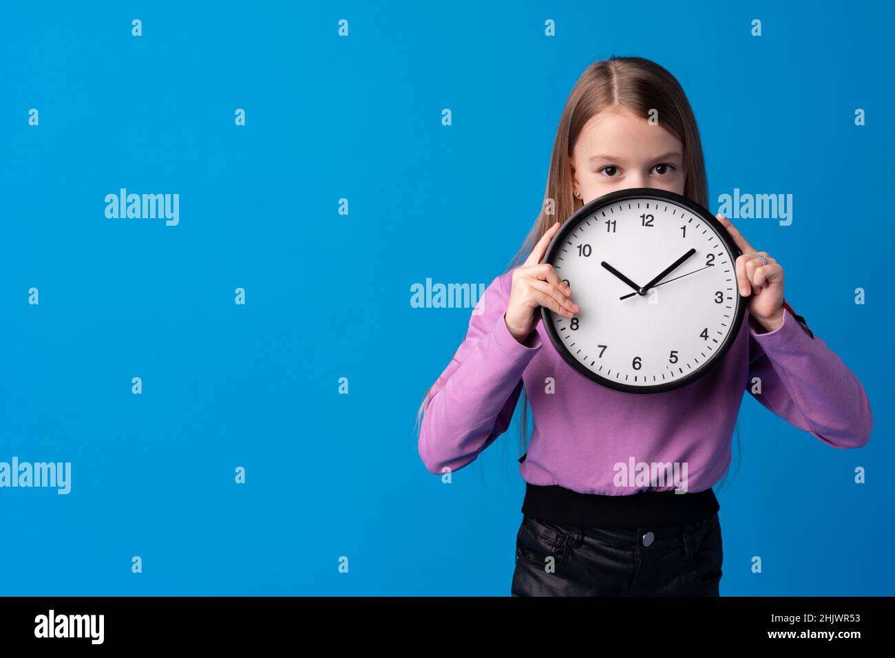 Beautiful teen girl holding wall clock over blue background Stock Photo ...