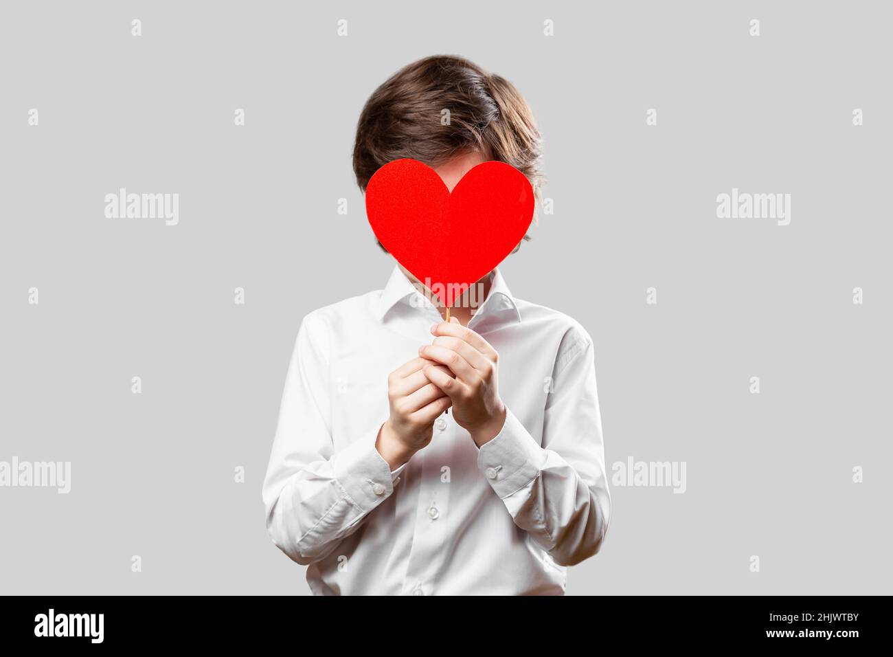 Boy hiding his face behind red st. valentines heart. Stylish young man ...