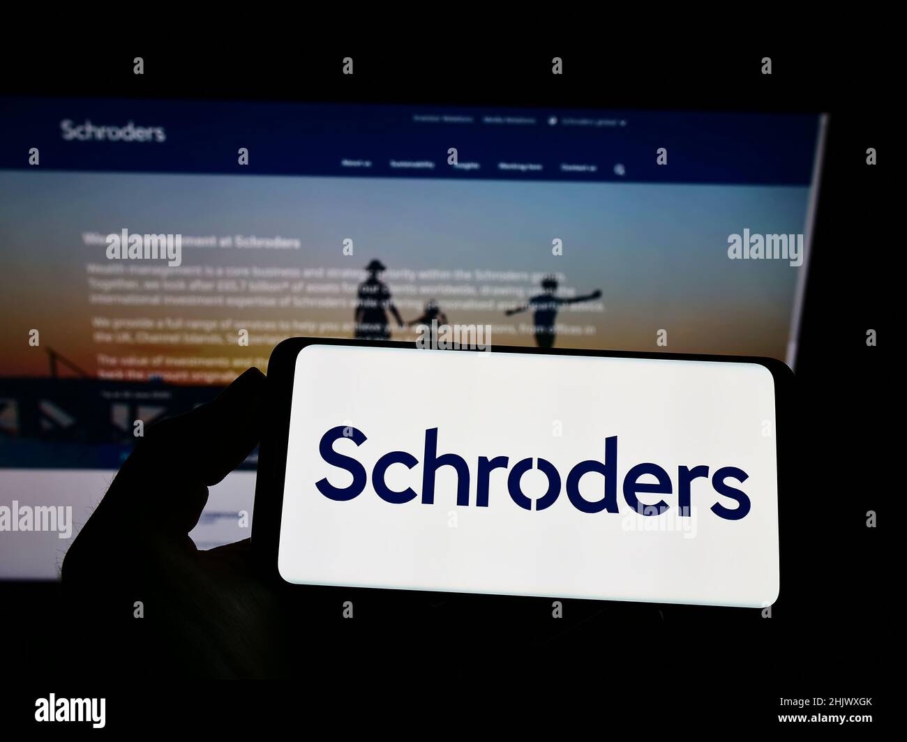 Person holding mobile phone with logo of British asset management ...