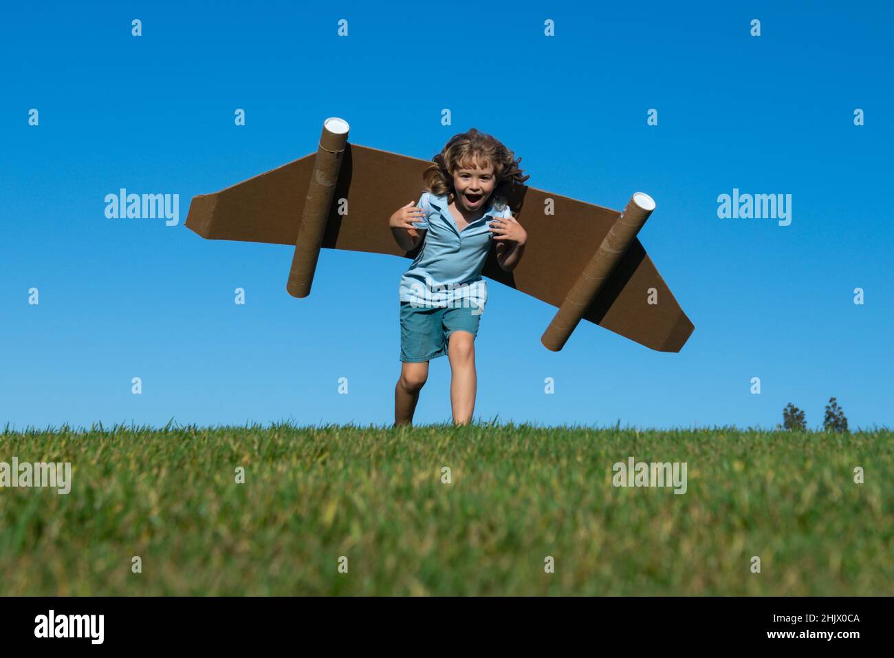 Happy child playing outside on green grass and blue sky. Kid pilot with ...
