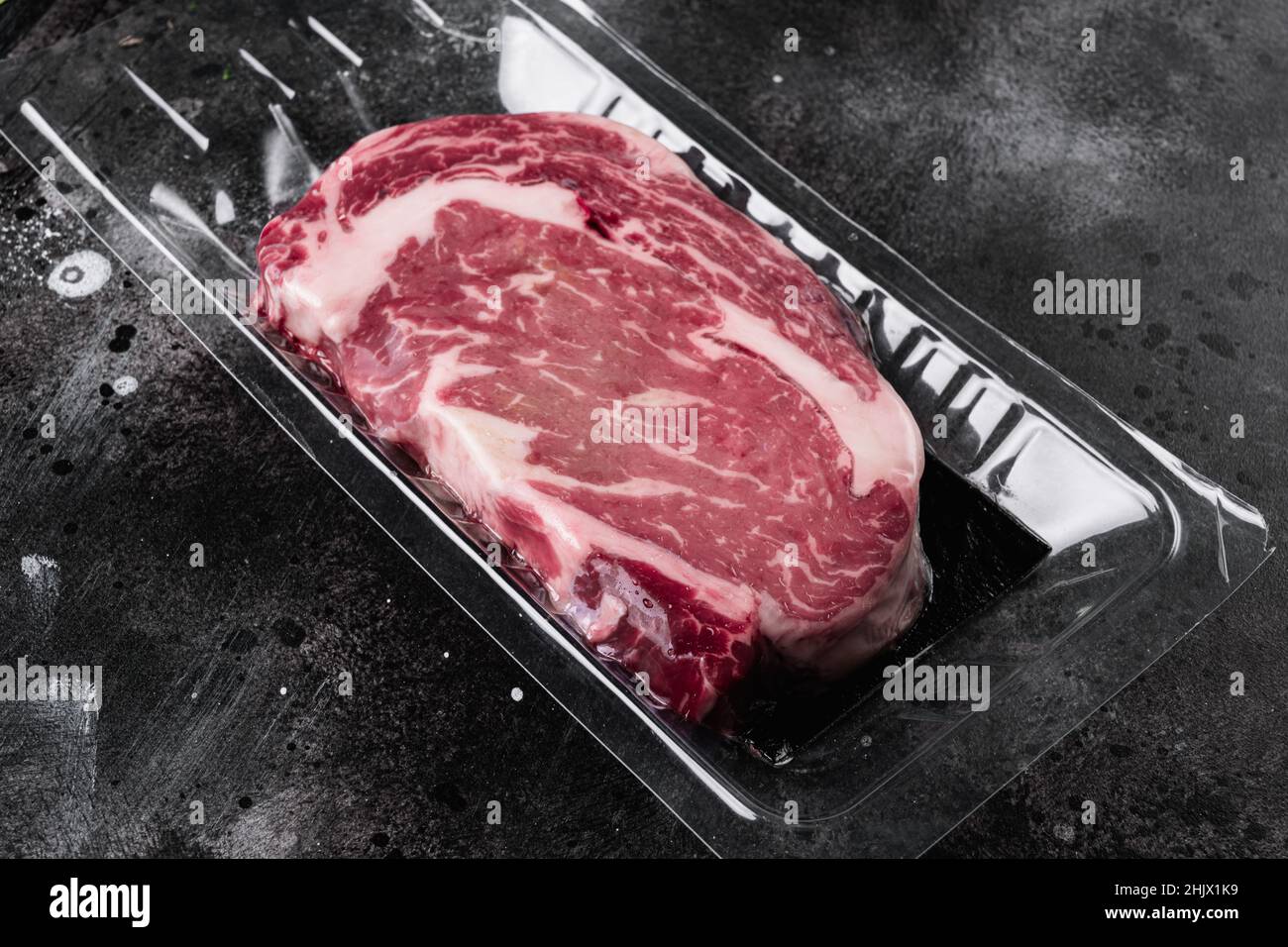 Packing raw beef steak in vacuum set, on black dark stone table ...