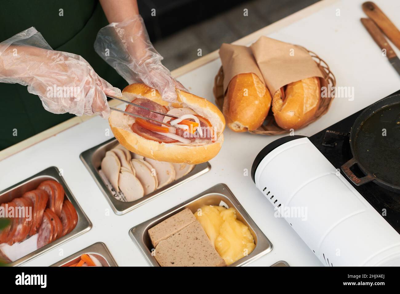 Hands of vendor putting meat and vegetables in cut bun, view from above ...