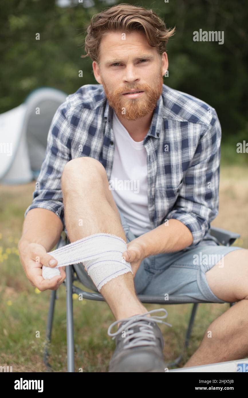 wounded man bandaging leg while on camping Stock Photo - Alamy