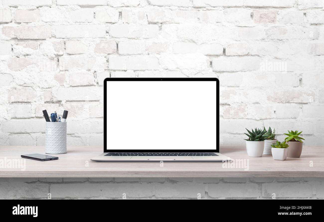 Laptop on office desk with isoalted screen for mockup. Plants, phone ...