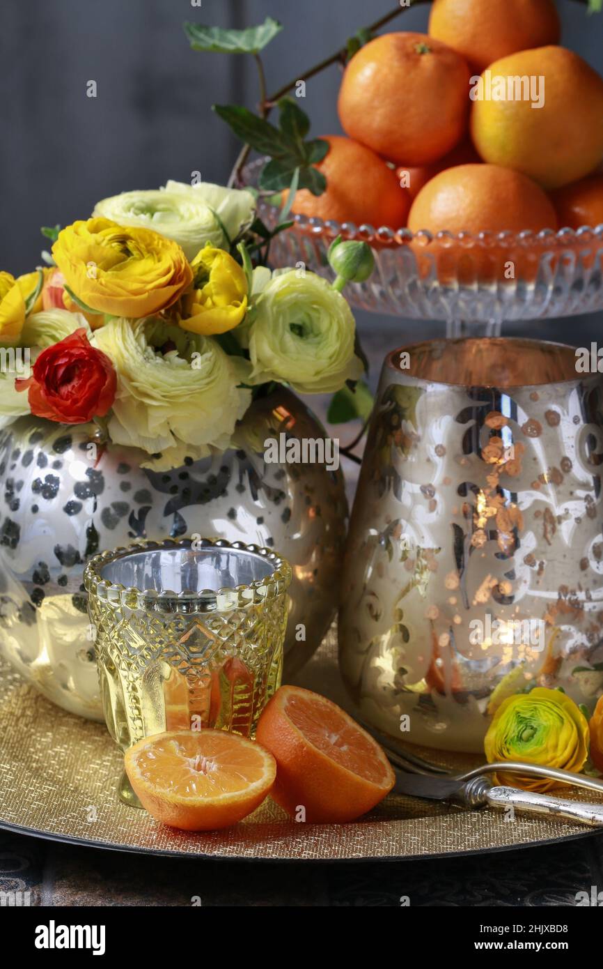 Bunch of ranunculus in a golden vase and a pile of sweet oranges. Party ...