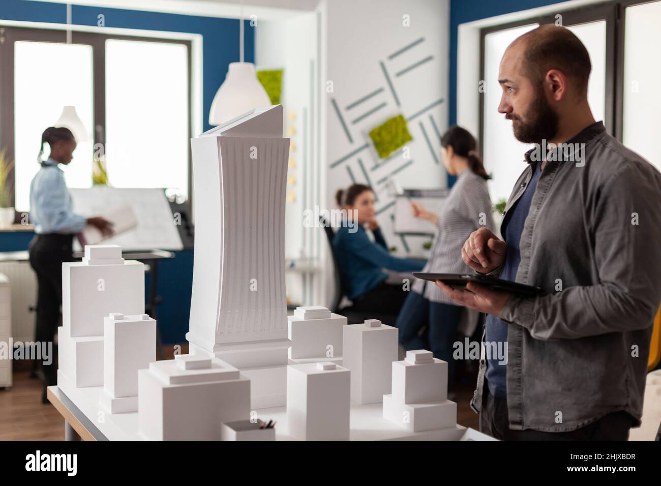 Architect Holding Tablet With Blueprints Inspecting Design Of White Foam Building Model In