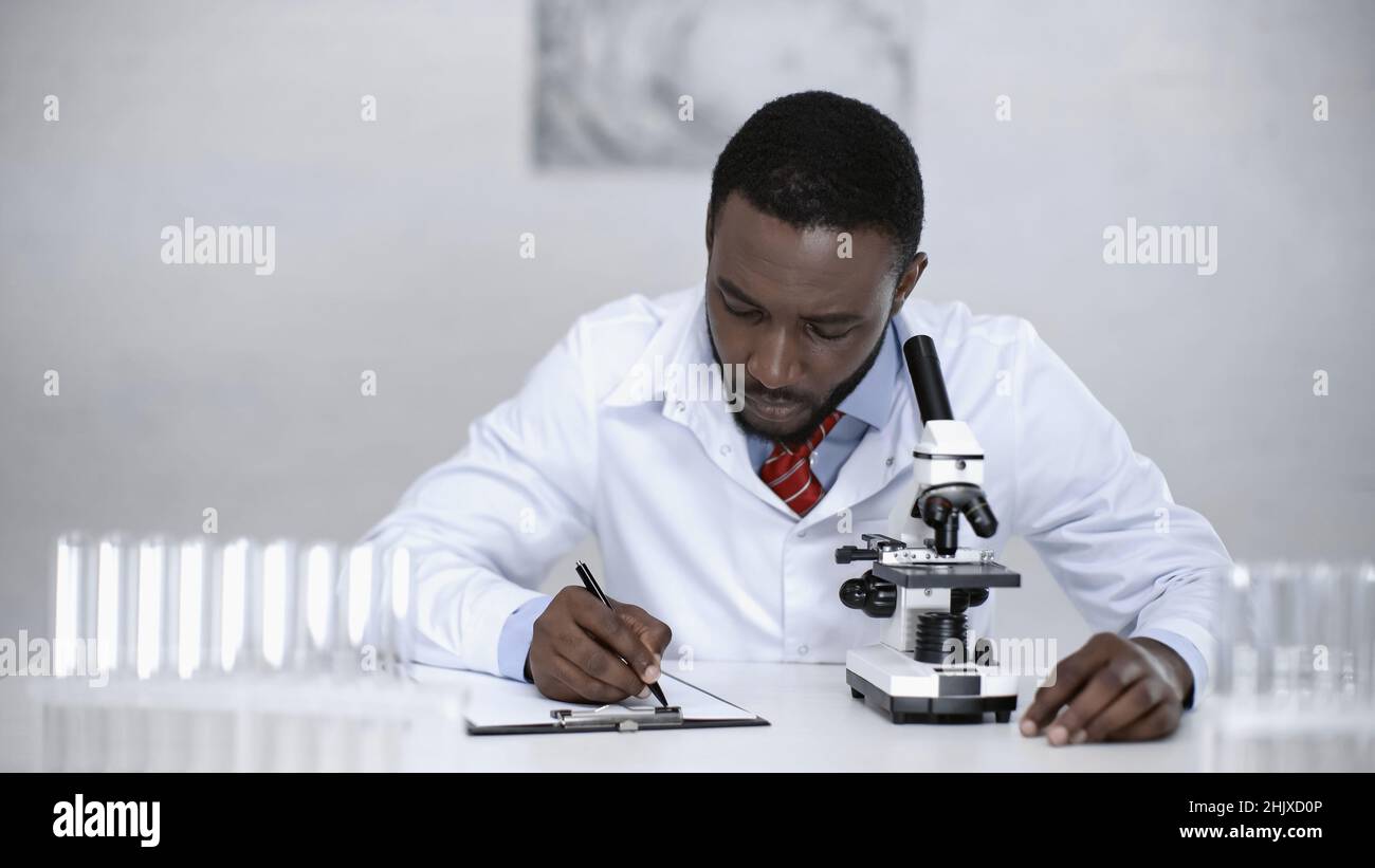 african american scientist writing on clipboard near microscope Stock ...