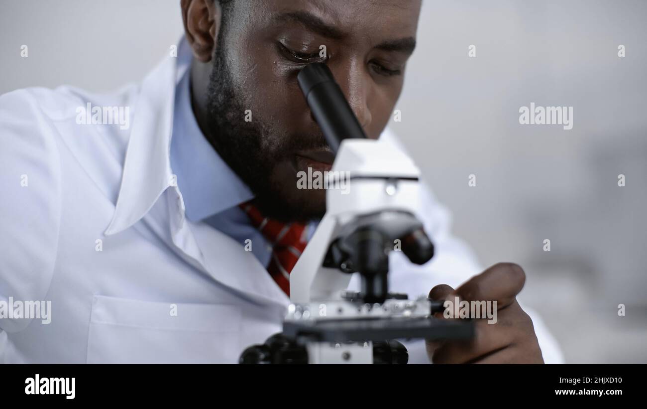 focused african american scientist looking through microscope in ...