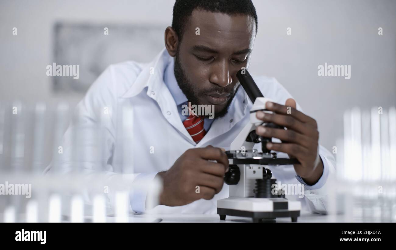 african american scientist in white coat looking through microscope in ...