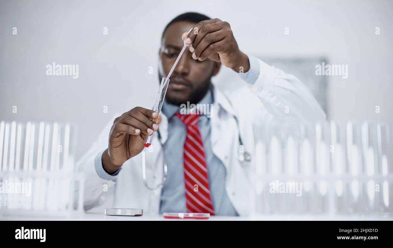 blurred african american scientist adding red liquid into test tube in ...