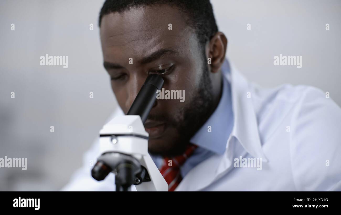 concentrated african american scientist looking through microscope in ...