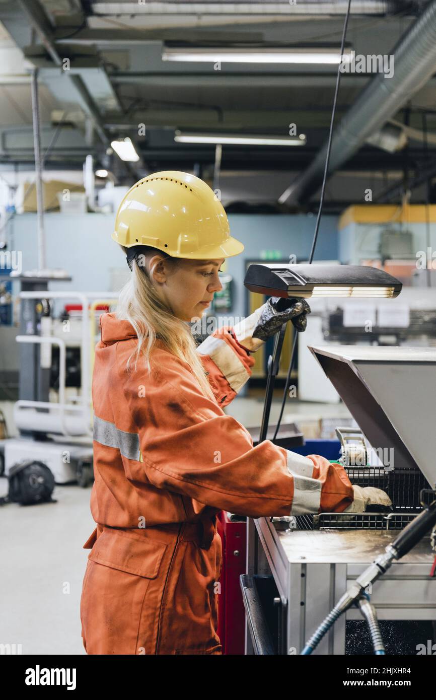 Young female industrial worker in uniform using manufacturing machinery ...