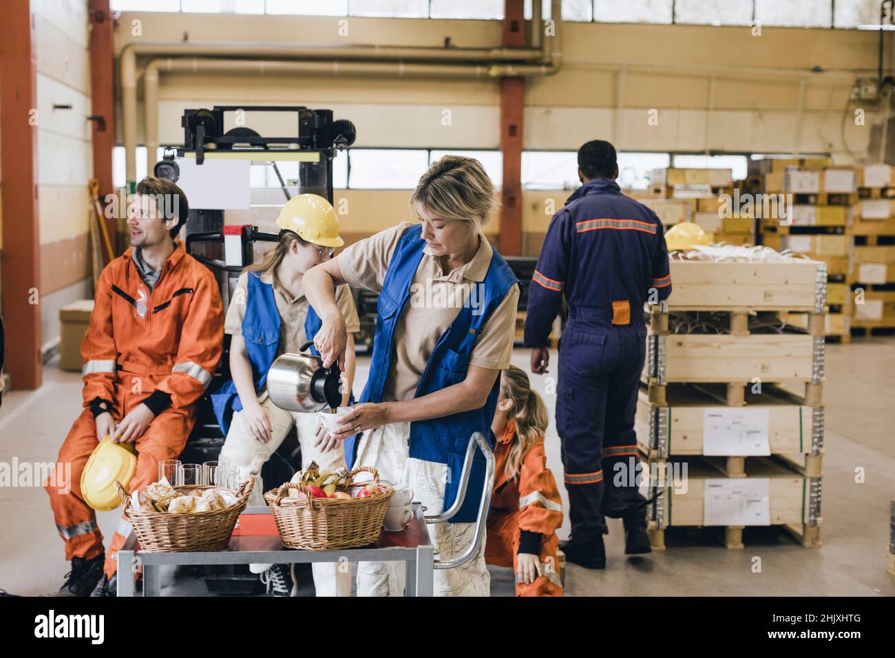 Female worker pouring coffee in cup while colleagues in background at ...