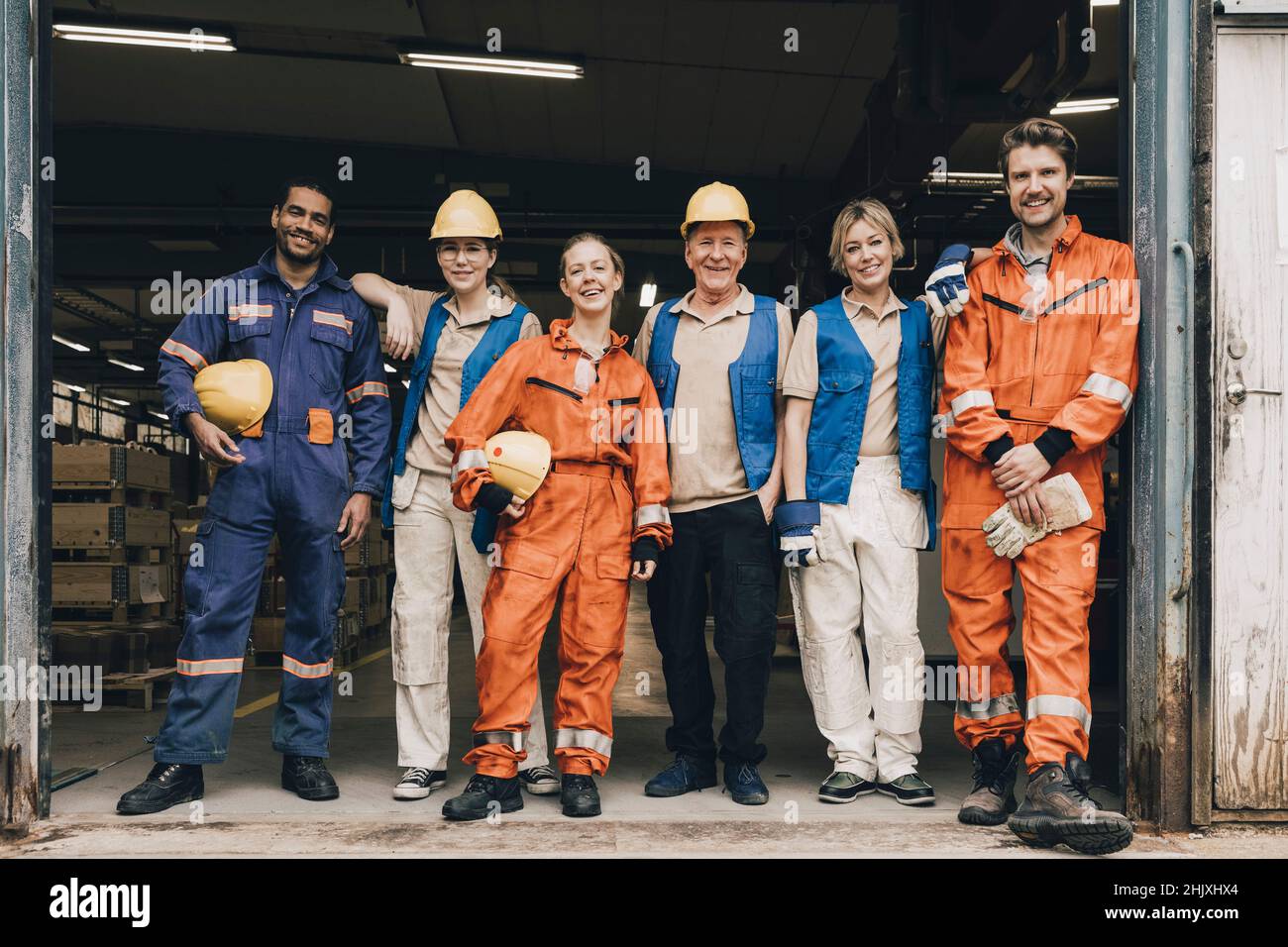Portrait of smiling male and female workers in workwear at entrance of ...