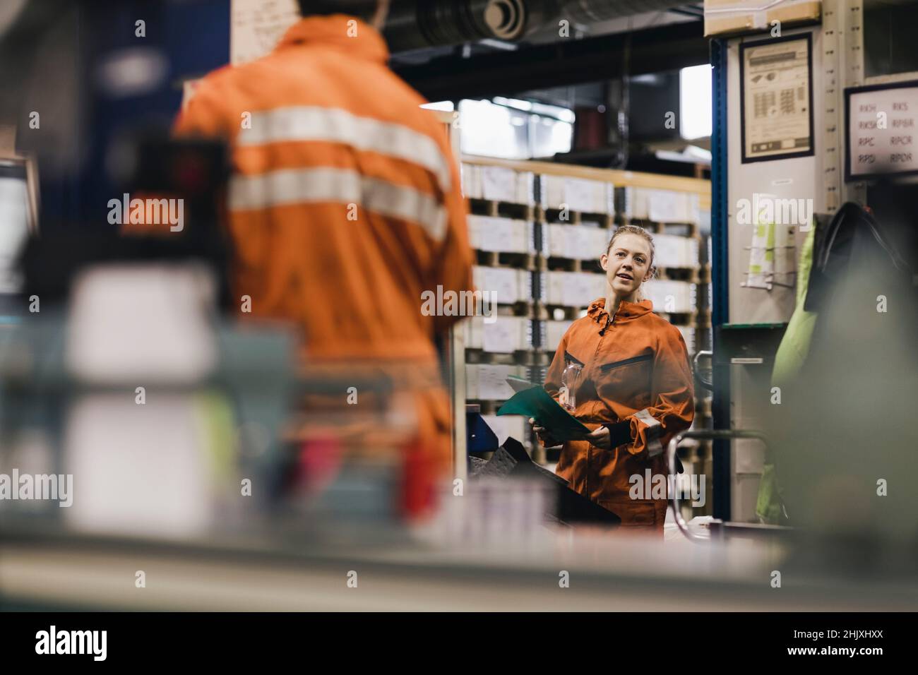 Female worker in uniform discussing with male coworker in factory Stock ...