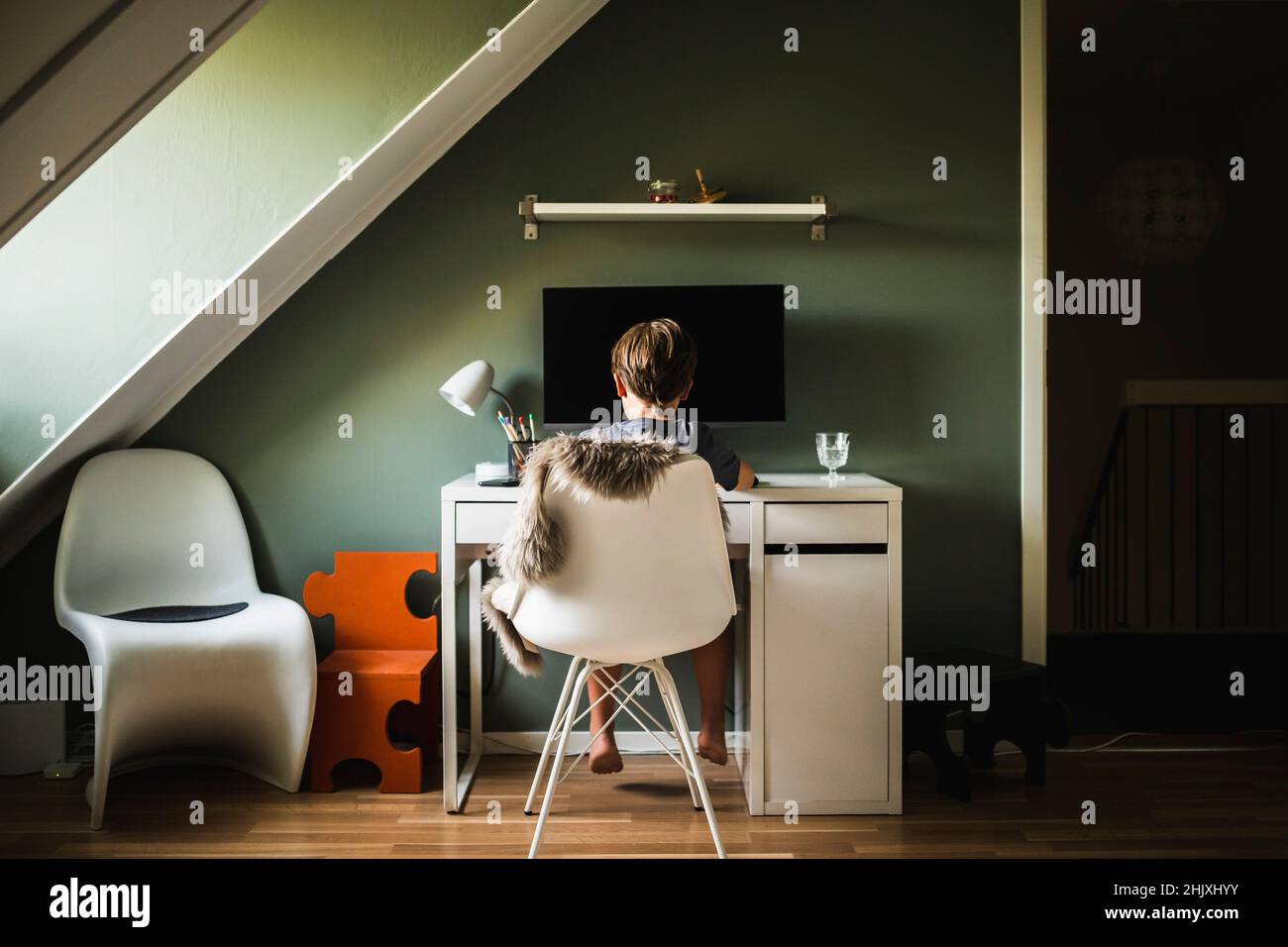 Rear view of boy sitting in front of computer at desk Stock Photo - Alamy