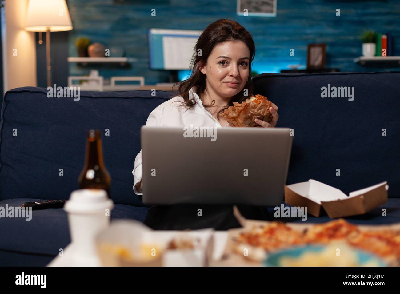 Programmer relaxing on couch holding laptop eating a tasty takeaway ...