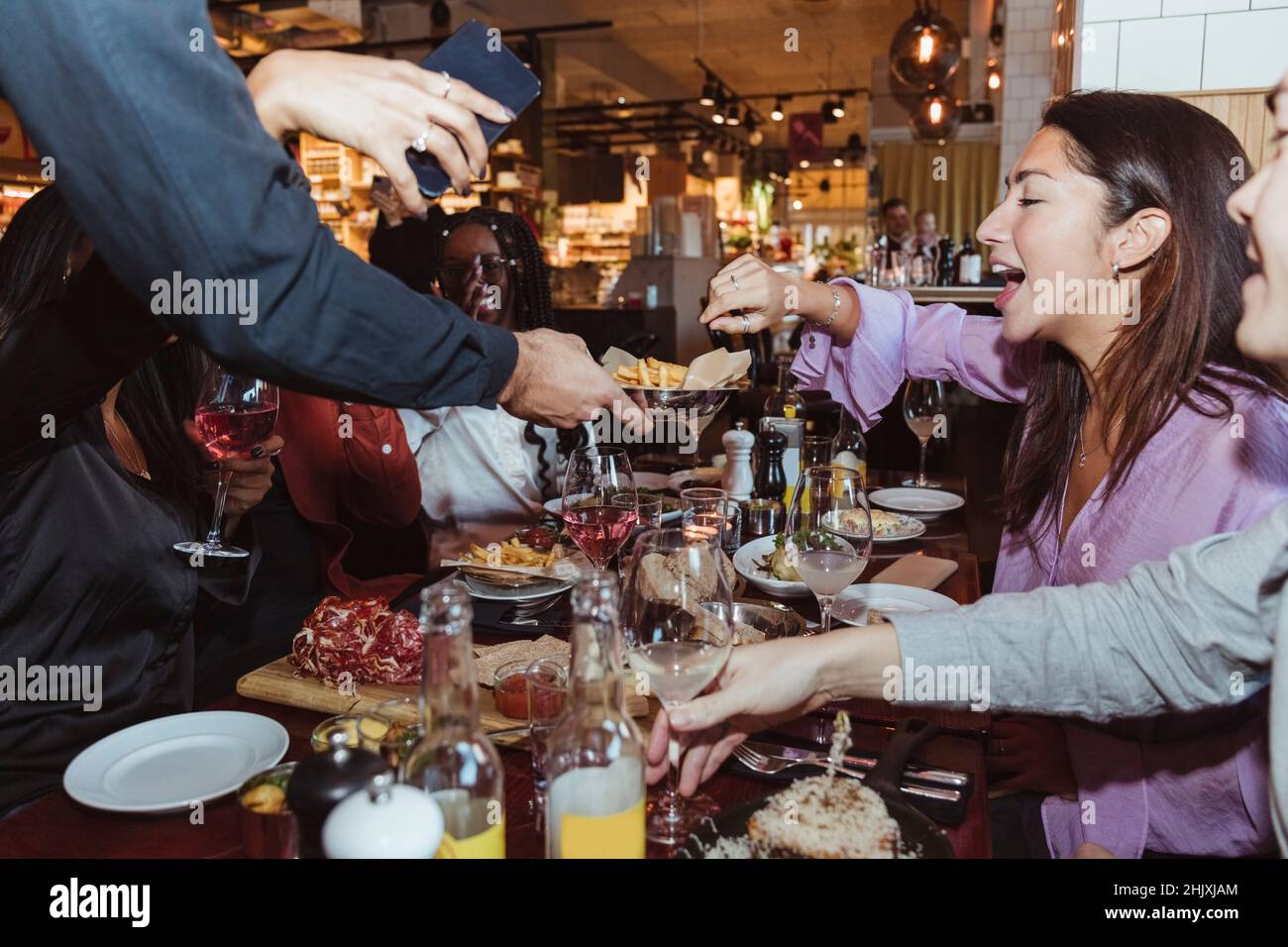 Cropped image of waiter serving food and drinks to customers at table ...