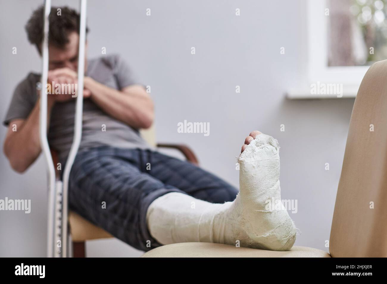 A sad man with a broken leg sits on a chair. Illness concept Stock ...