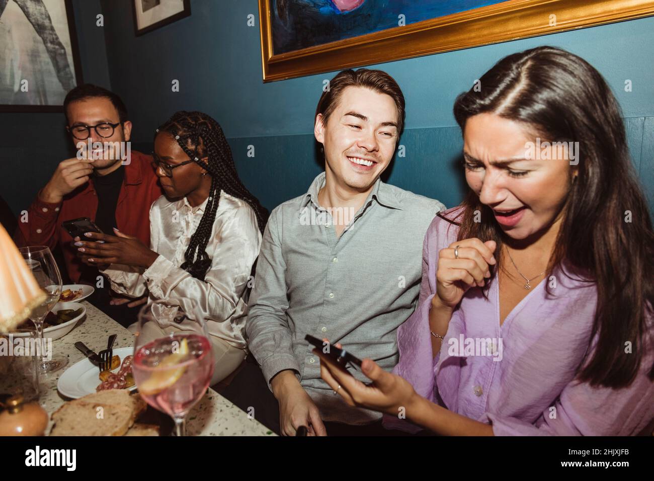 Happy women using smart phone while sitting by male friends at ...