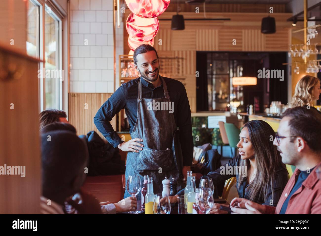 Smiling waiter talking with male and female friends in restaurant ...