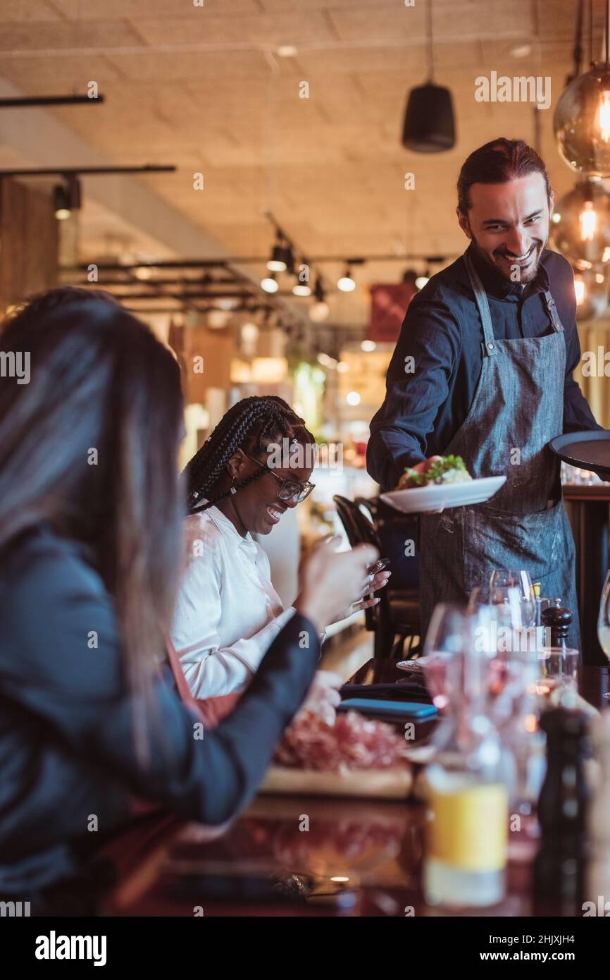 Happy waiter serving food to female customers in restaurant Stock Photo ...