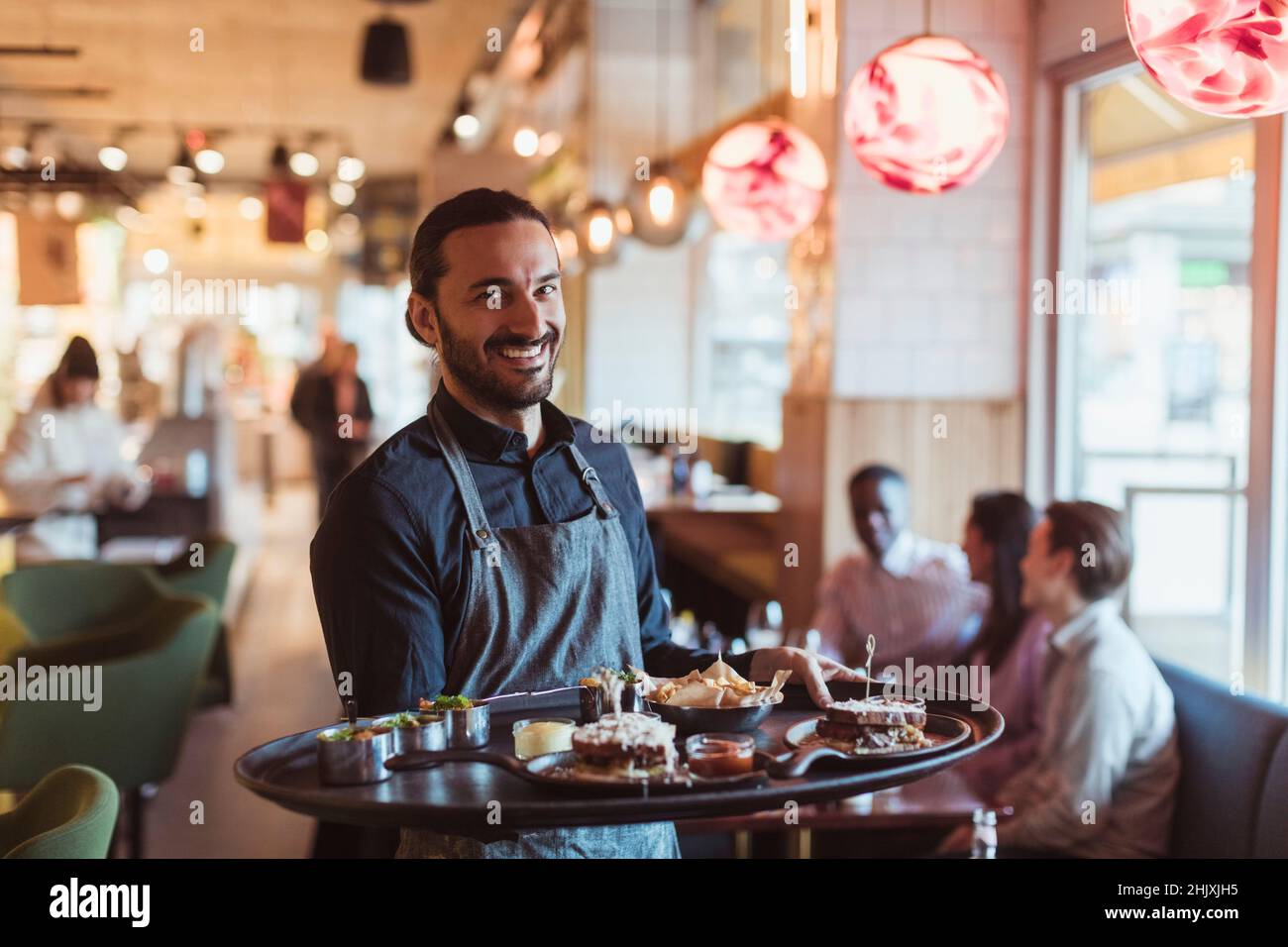 Portrait of smiling waiter with food while customer sitting in ...