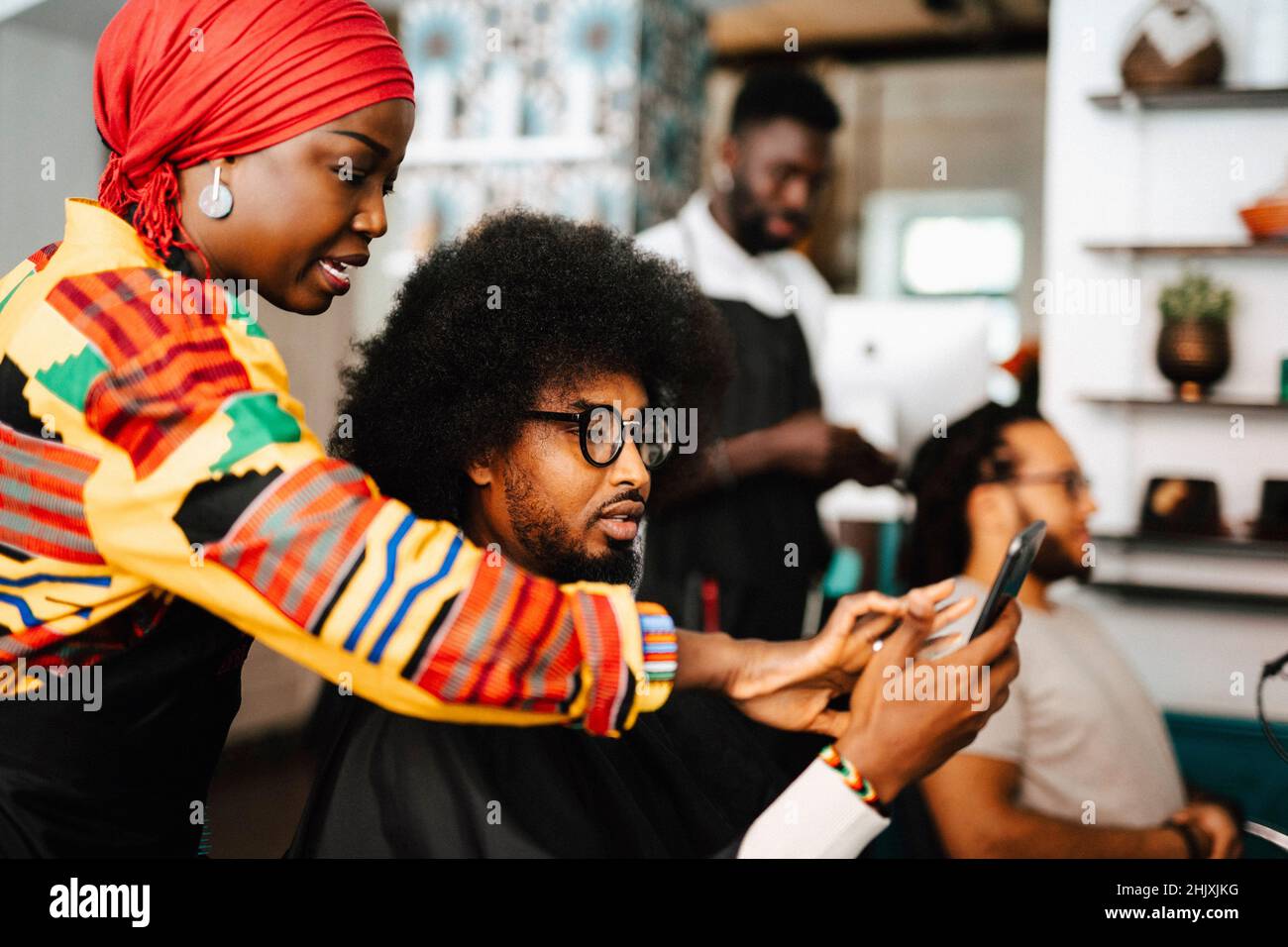 Female hairdresser using smart phone of male customer in barber shop ...