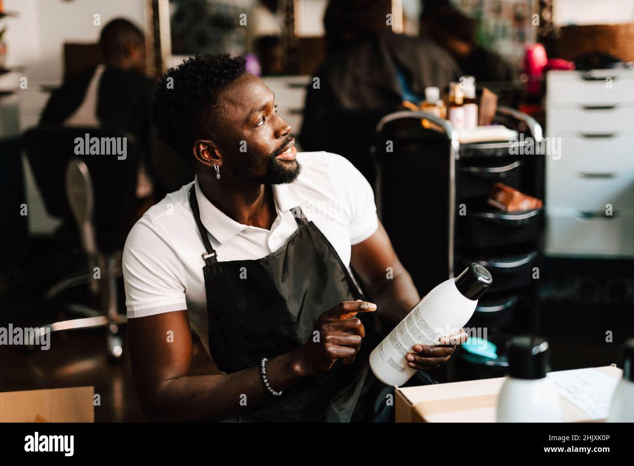 Male barber with beauty product looking away in hair salon Stock Photo ...