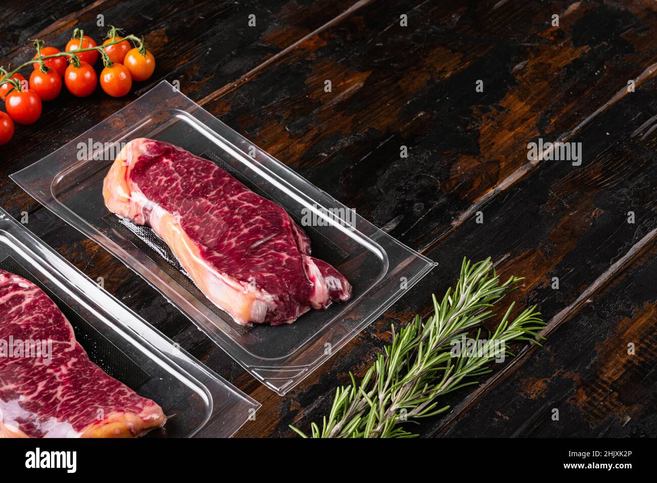 Raw marbled beef steaks in vacuum pack set, on old dark wooden table background, with copy space ...