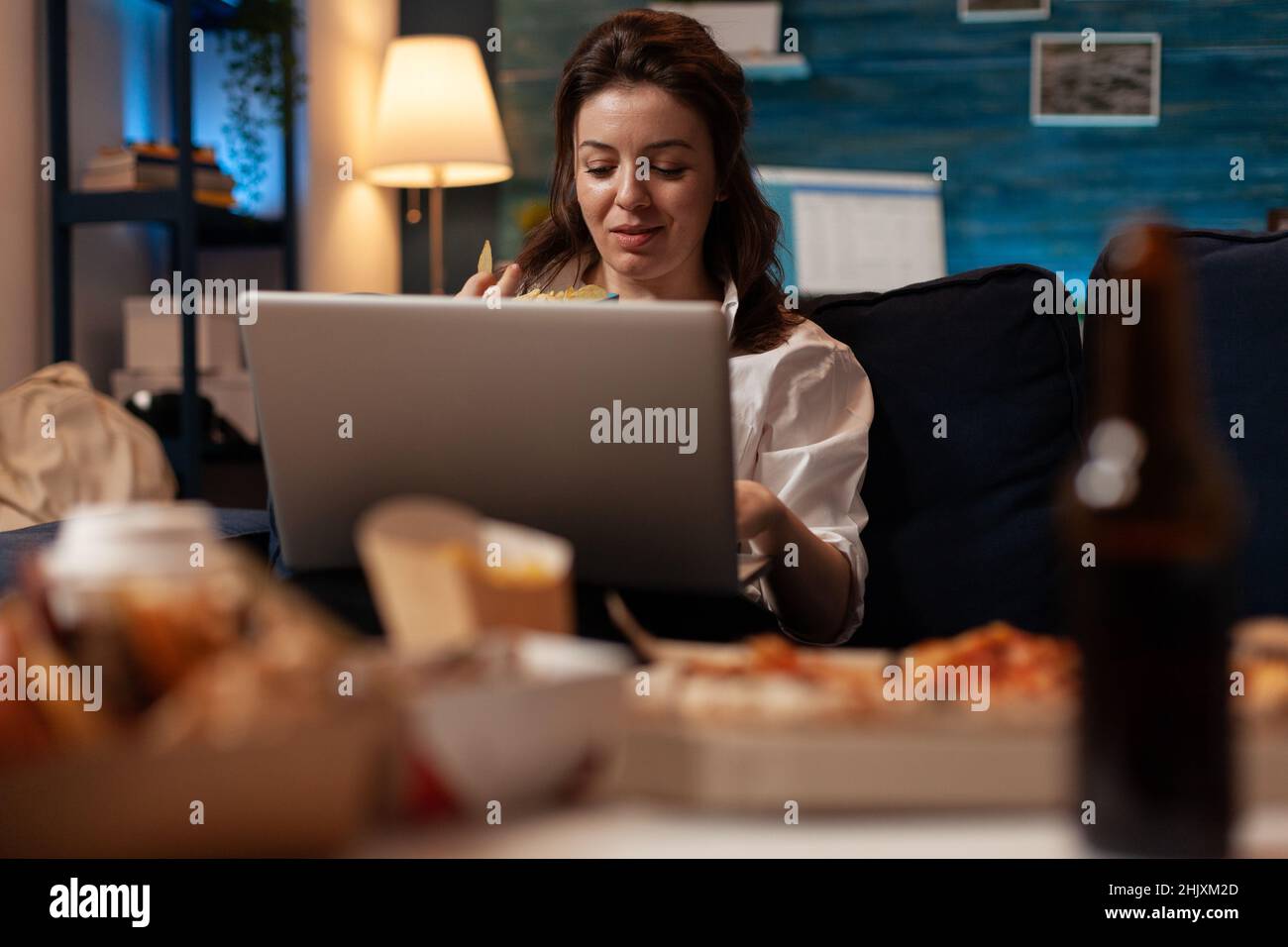 Woman browsing social media on laptop while having fast food snack ...