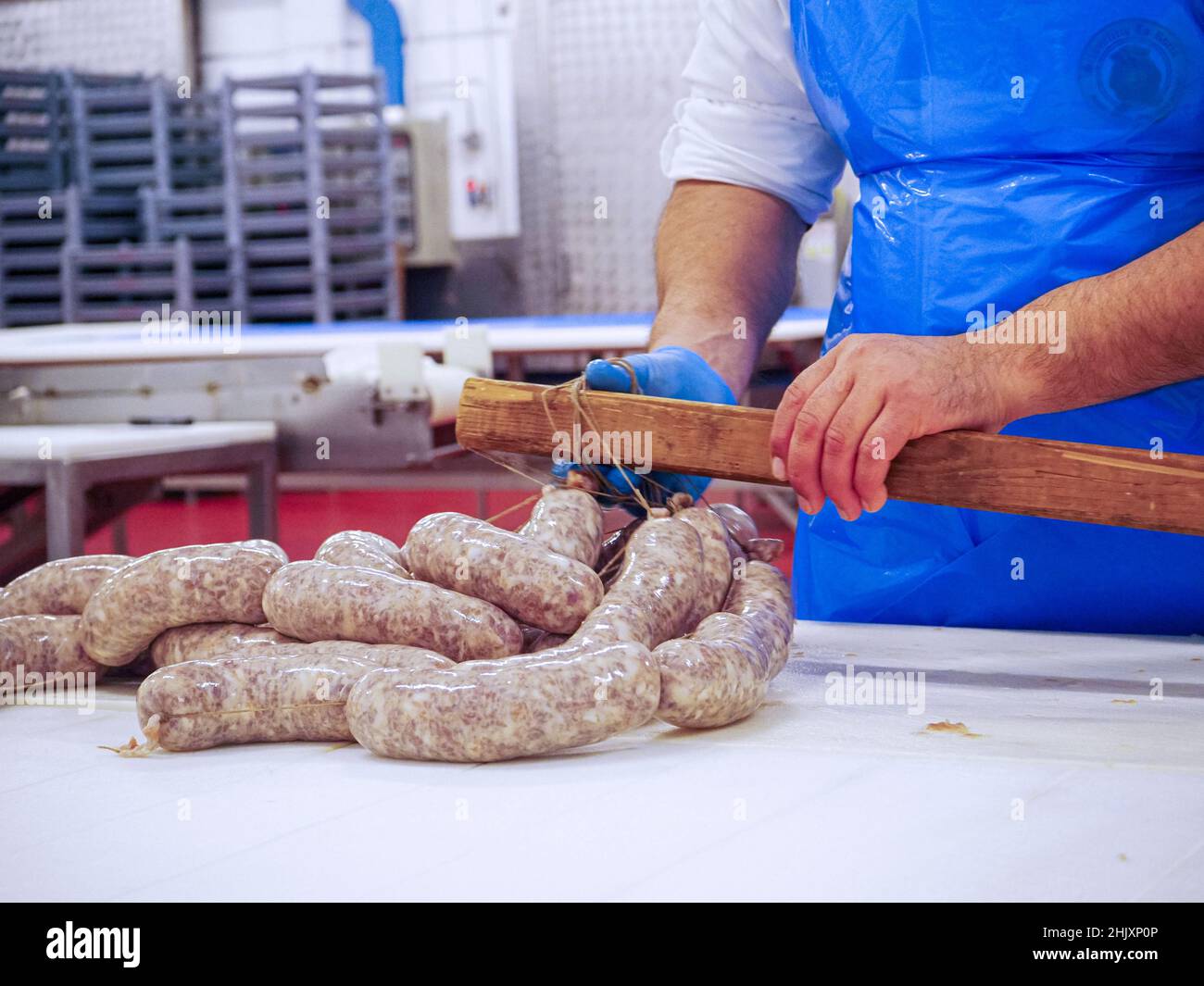 worker manufacturing, stuffing and tying pork sausages, salami and ...