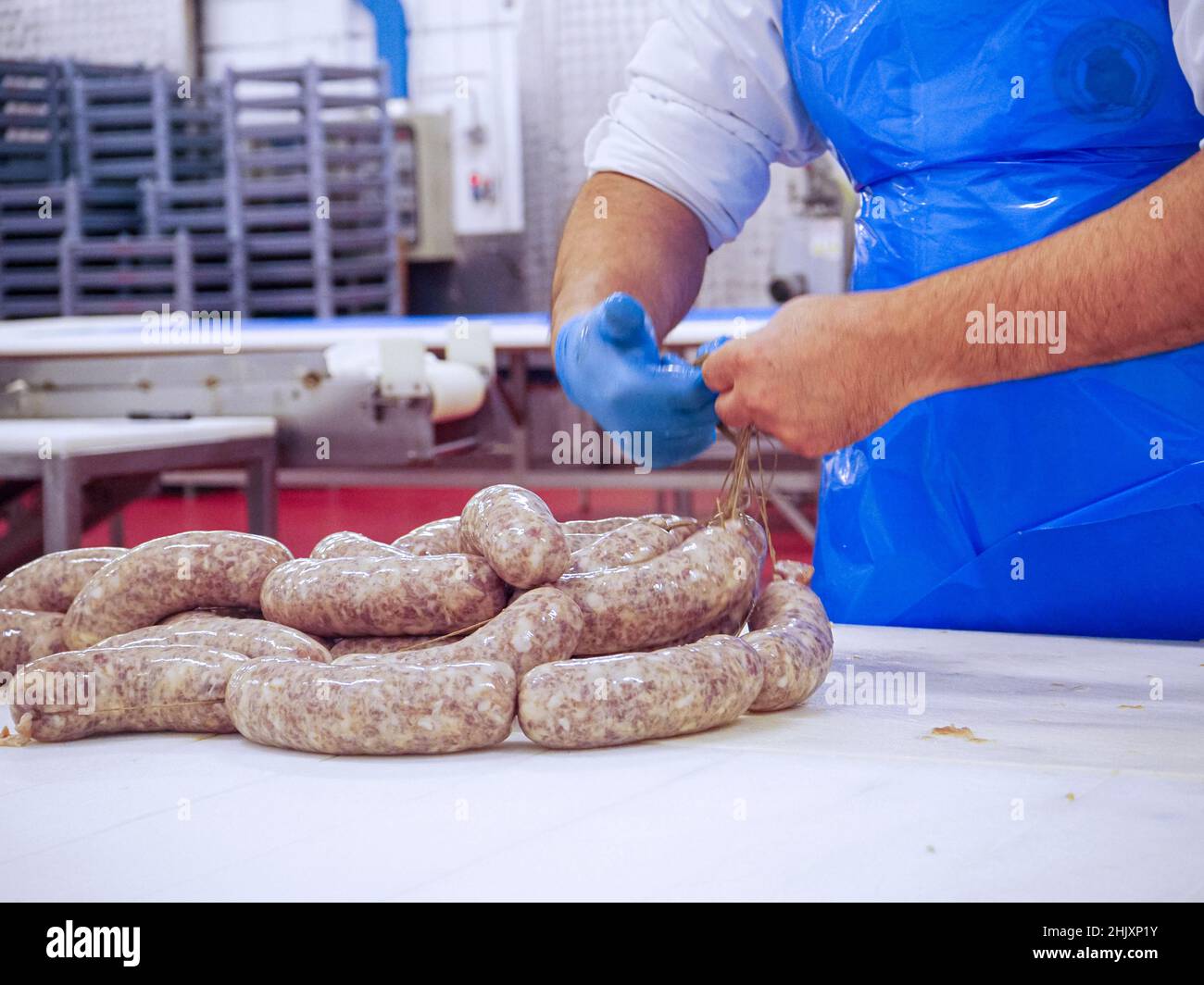 worker manufacturing, stuffing and tying pork sausages, salami and ...