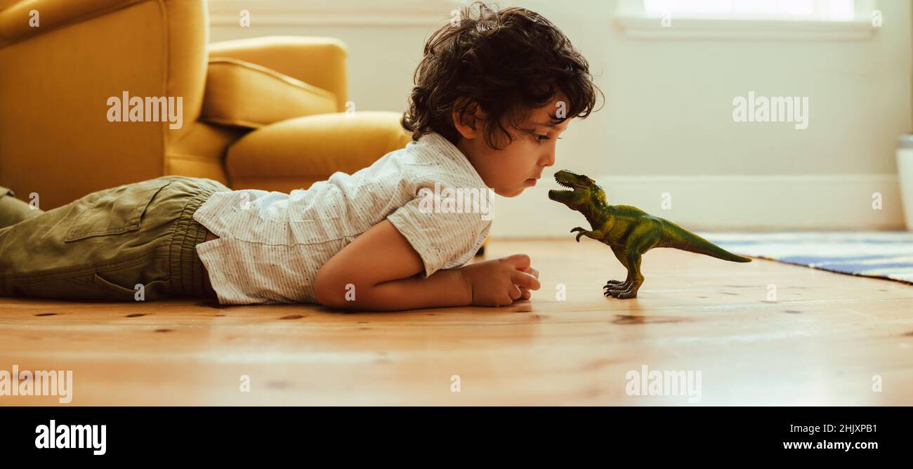 Cute young boy looking at his dinosaur toy at home. Adorable little boy ...
