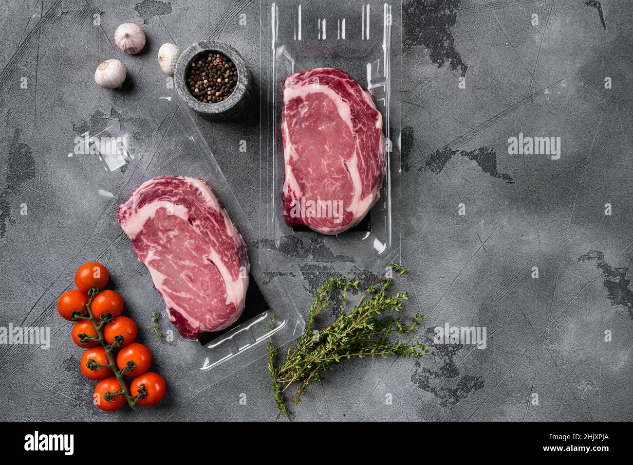 Rib-eye beef steak in plastic packing tray set, on gray stone table ...