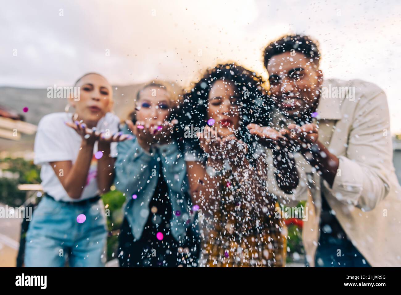 Confetti celebrations on the rooftop. Group of vibrant friends blowing ...