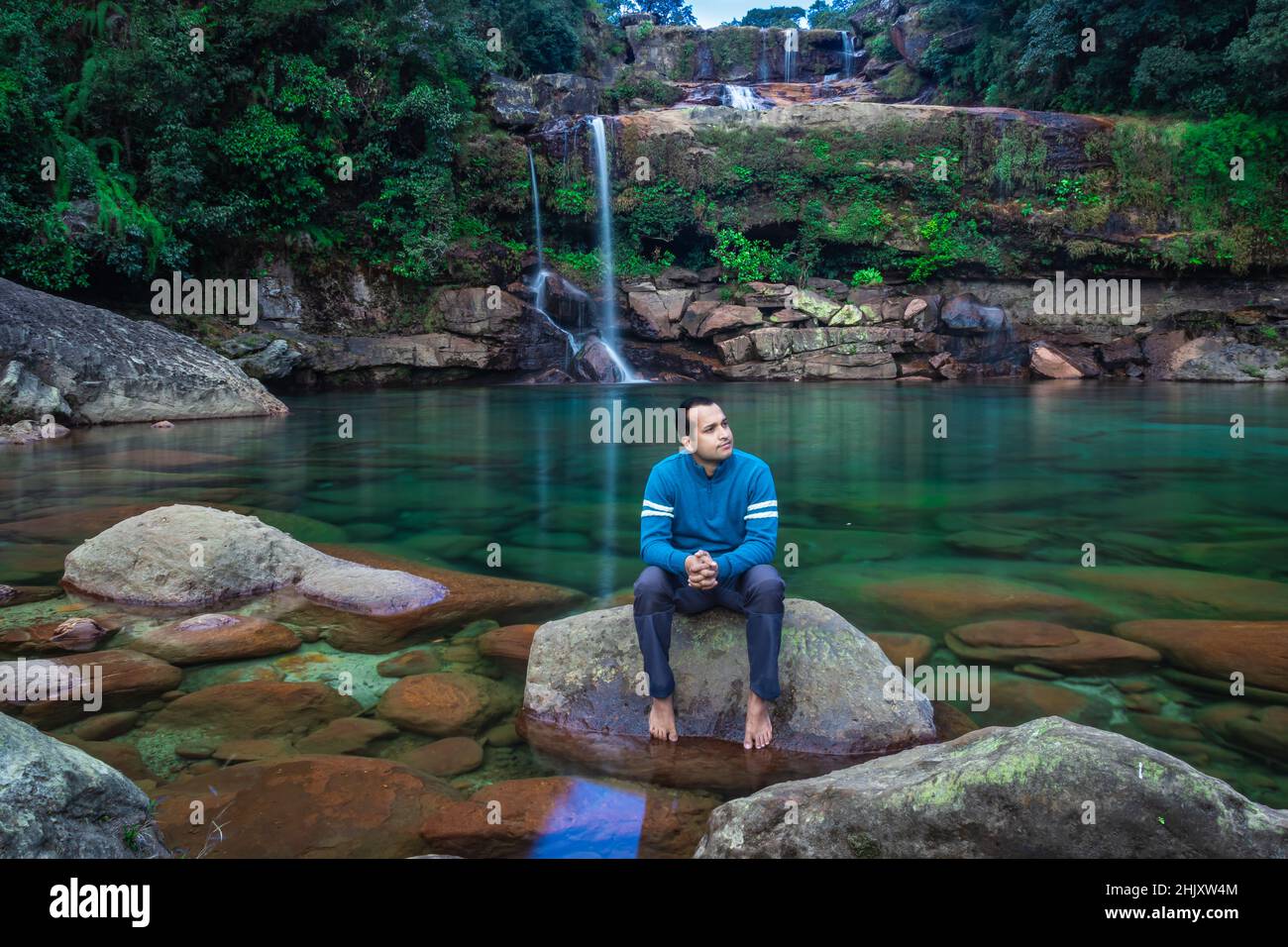 young man isolated sitting on rock with pristine waterfall background ...