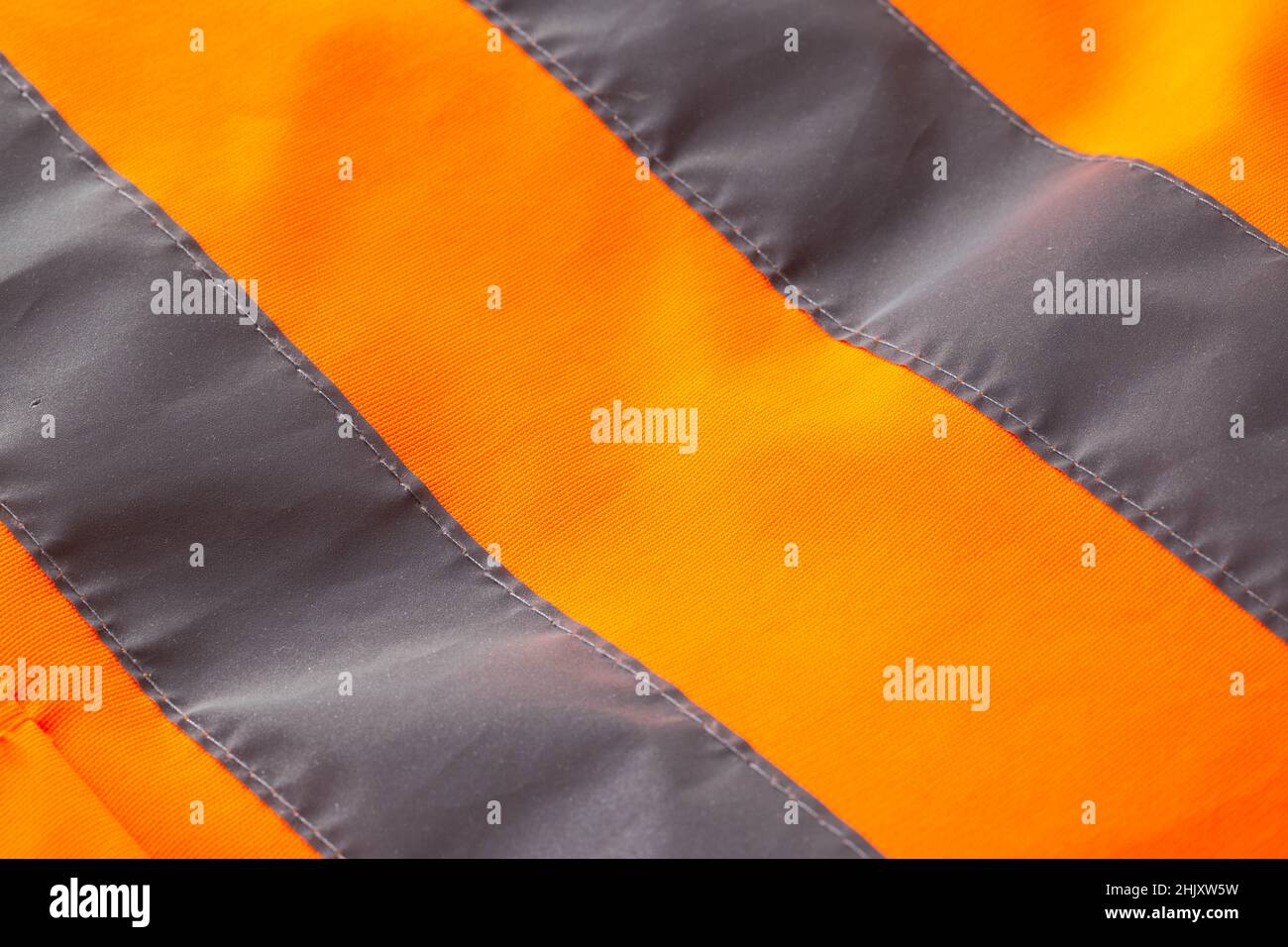 Orange signal vest with silver reflective stripes, background. Macro ...