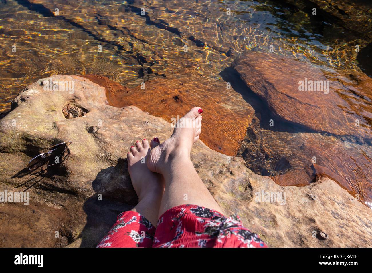 young girl feet relaxing and sunglasses on rock at the edge of river ...