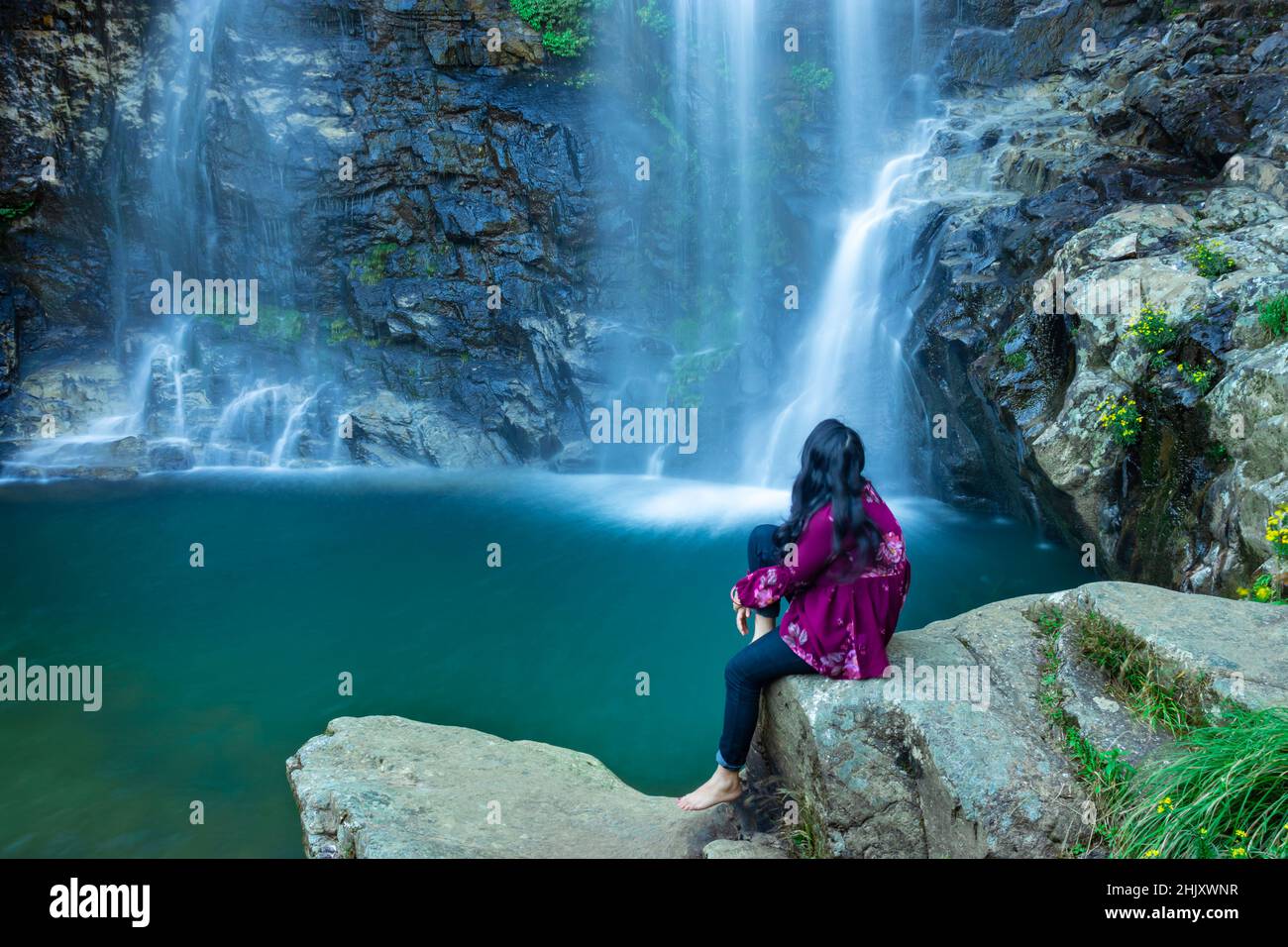young girl watching waterfall falling from mountain with calm blurred ...